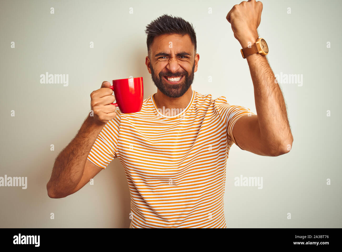 Young indian man drinking red cup of coffee standing over isolated ...