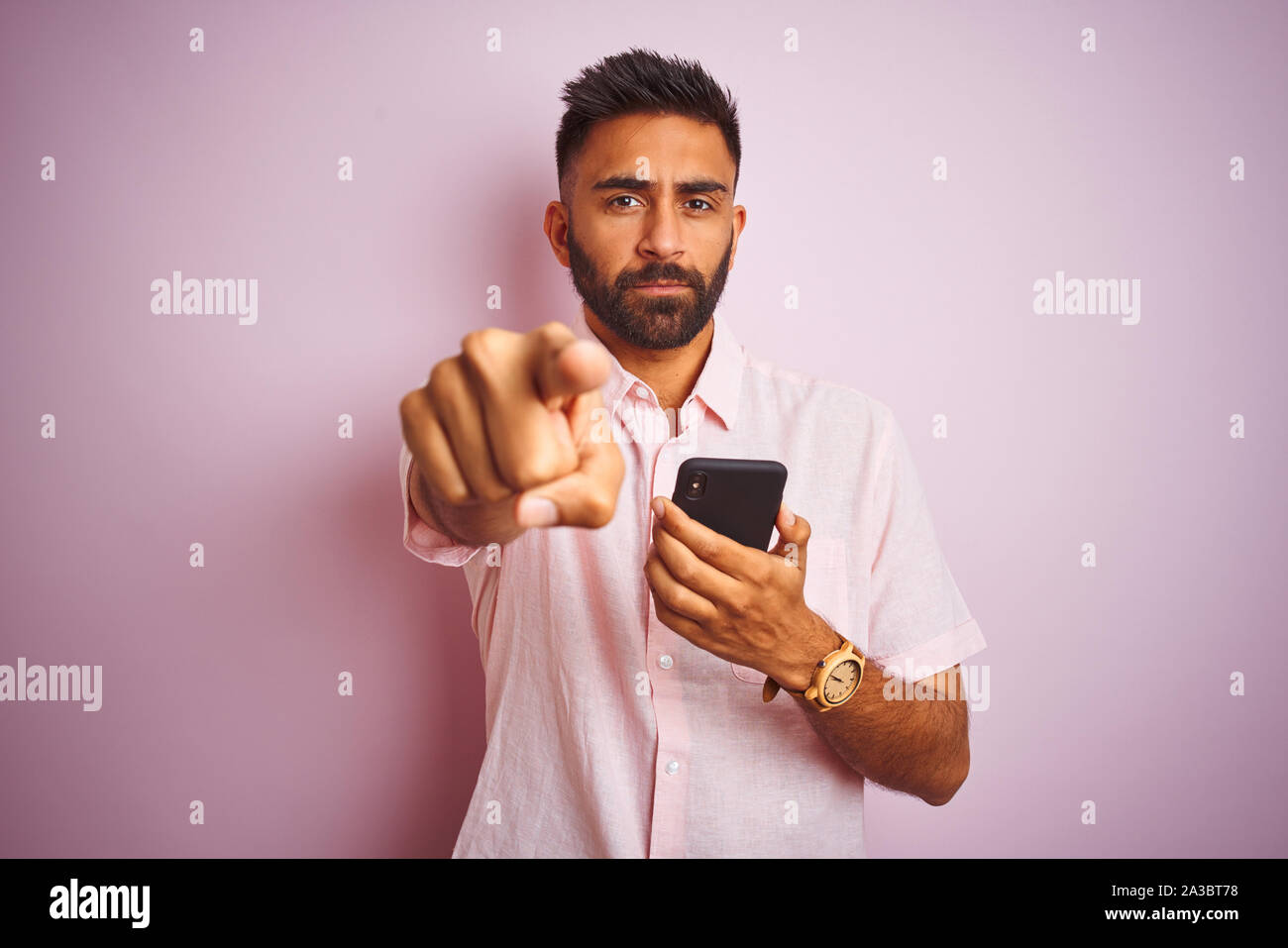 Young indian man using smartphone standing over isolated pink ...