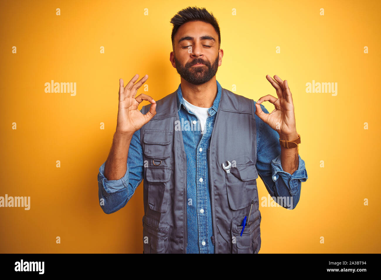 Handsome indian technician man wearing uniform over isolated yellow ...