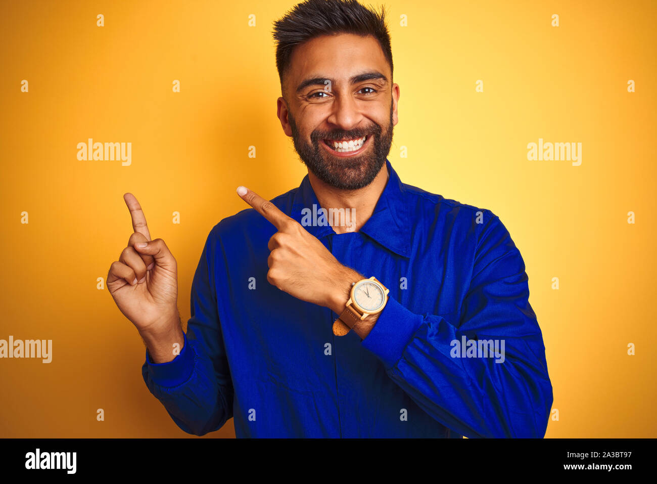 Handsome indian worker man wearing uniform over isolated yellow ...