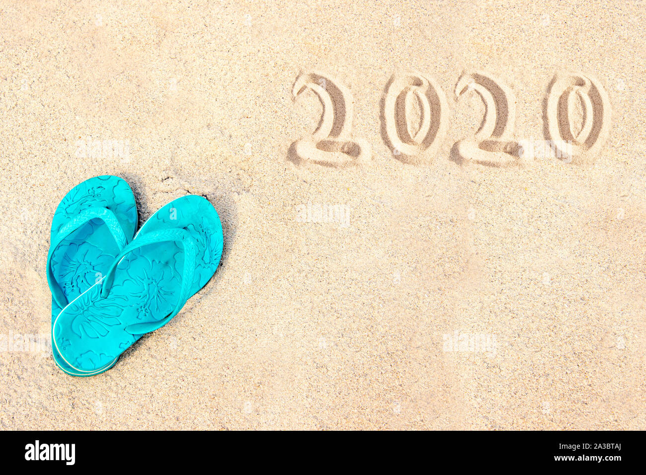 Blue pair of flip flops on the beach, 2020 written in the sand ...