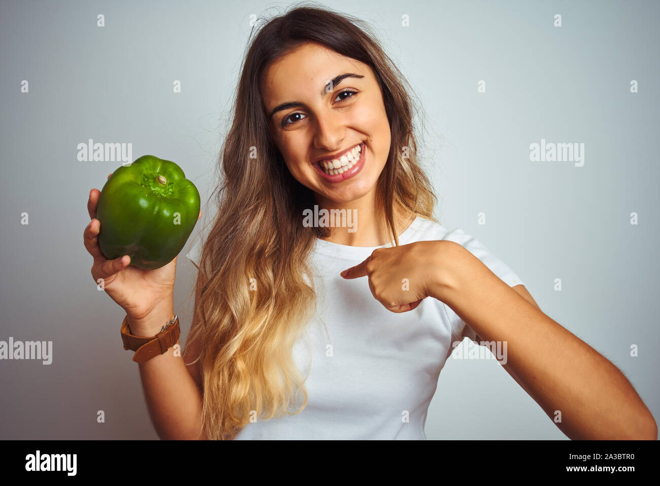 Young beautiful woman holding green pepper over white isolated ...