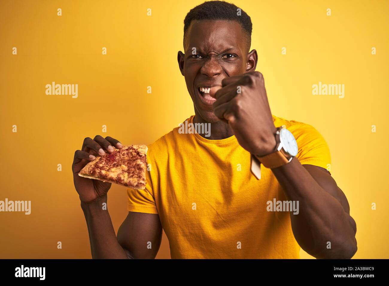 African american man eating slice of pizza standing over isolated ...