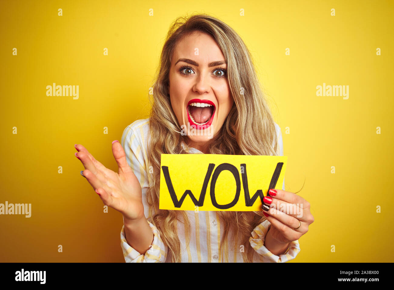 Beautiful woman holding amazed wow surprise banner over isolated yellow ...