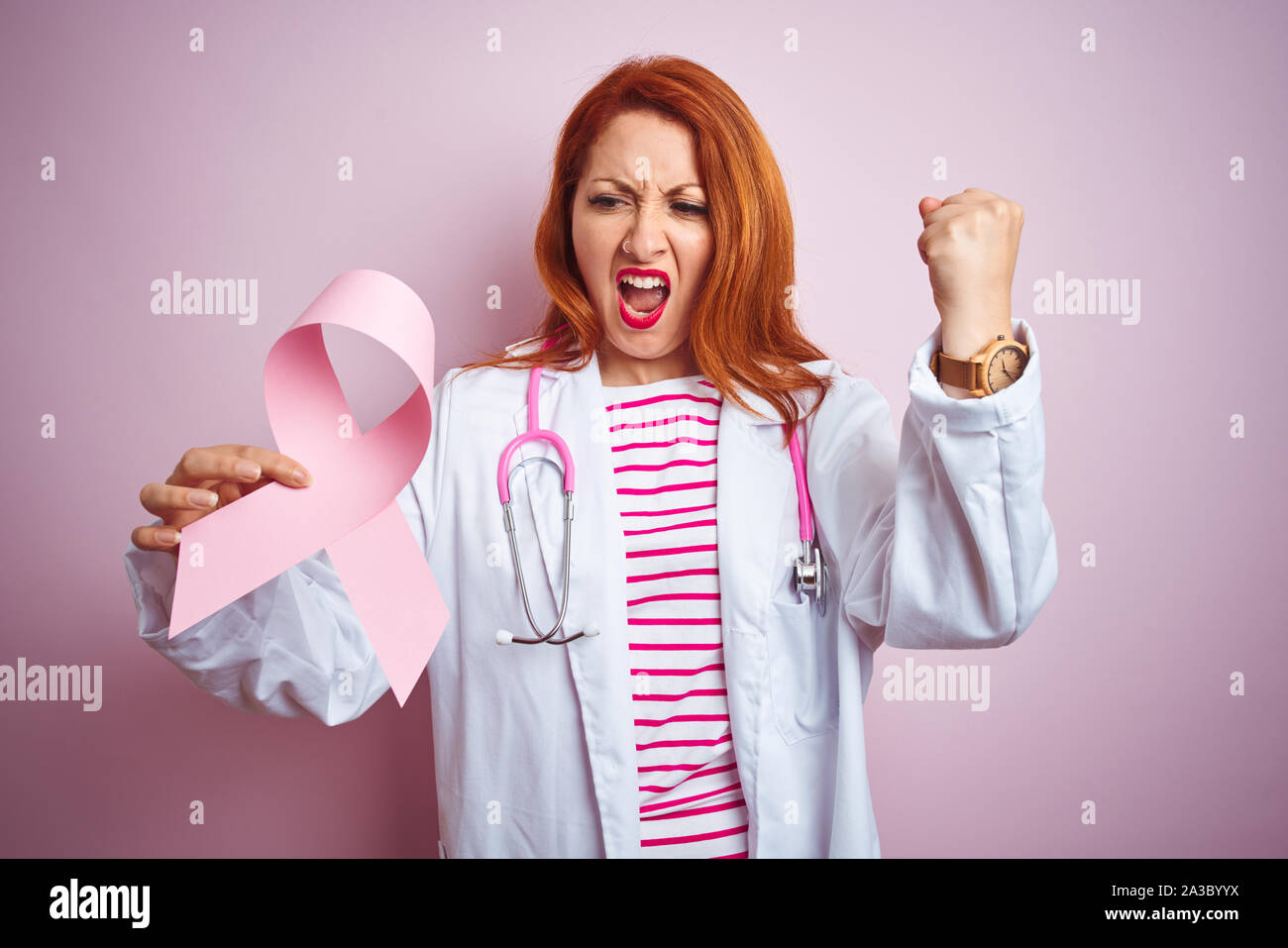 Young redhead doctor woman holding cancer ribbon over pink isolated ...