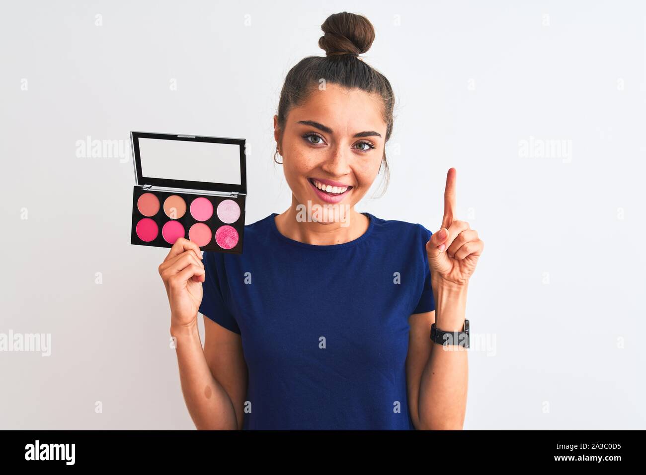 Young beautiful woman holding makeup standing over isolated white ...