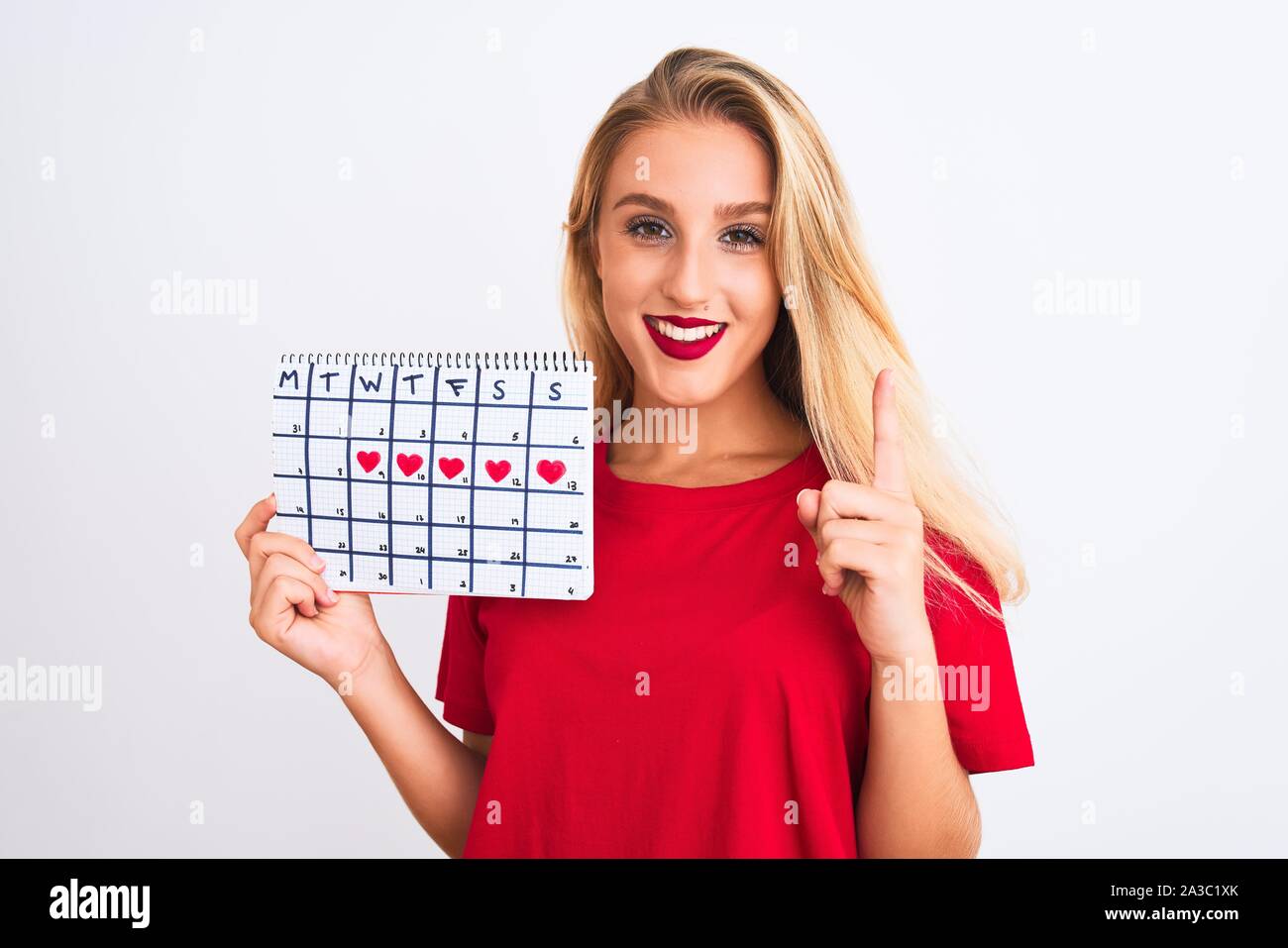 Young beautiful woman holding period calendar standing over isolated ...