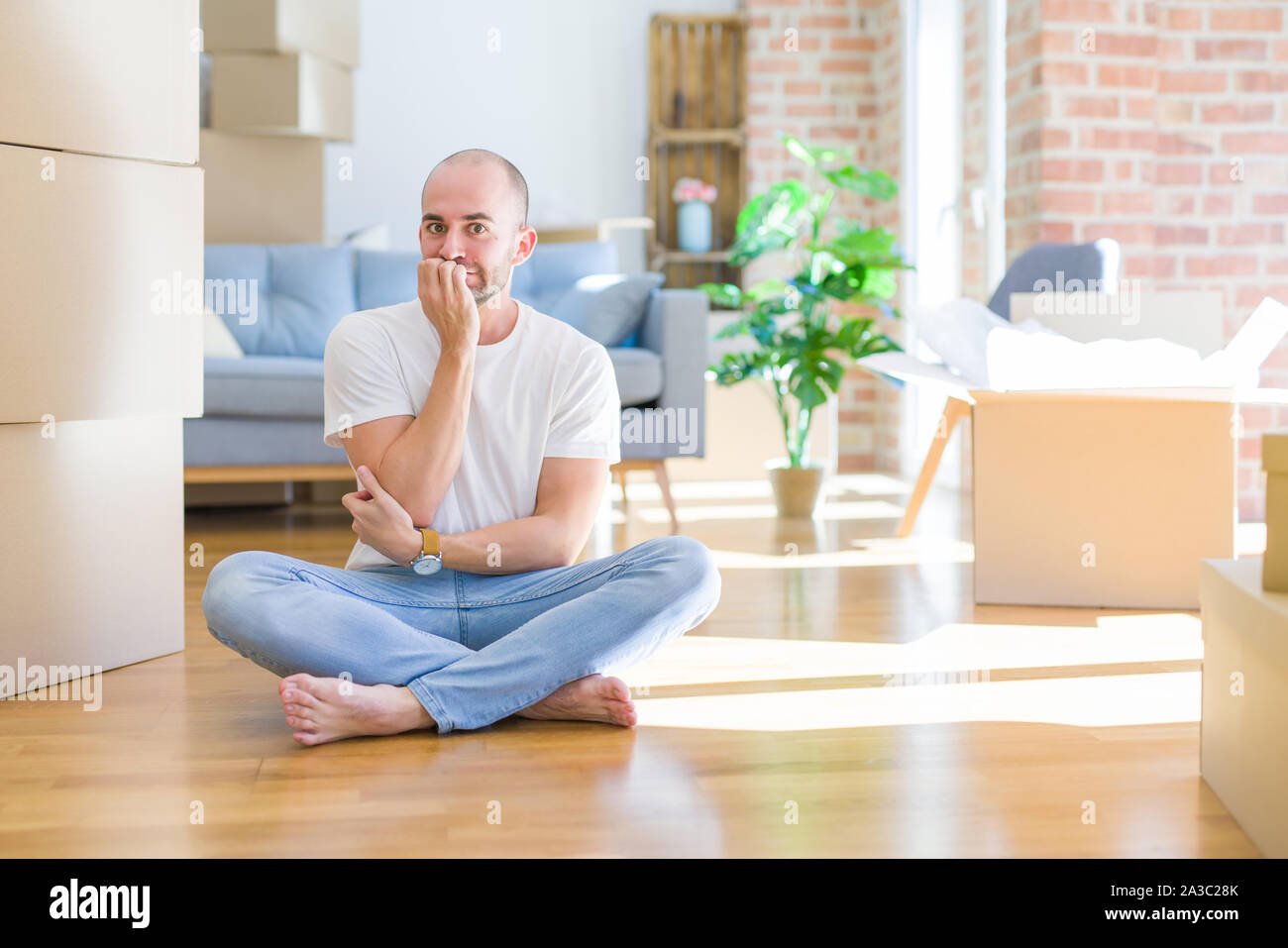 Young bald man sitting on the floor around cardboard boxes moving to a ...