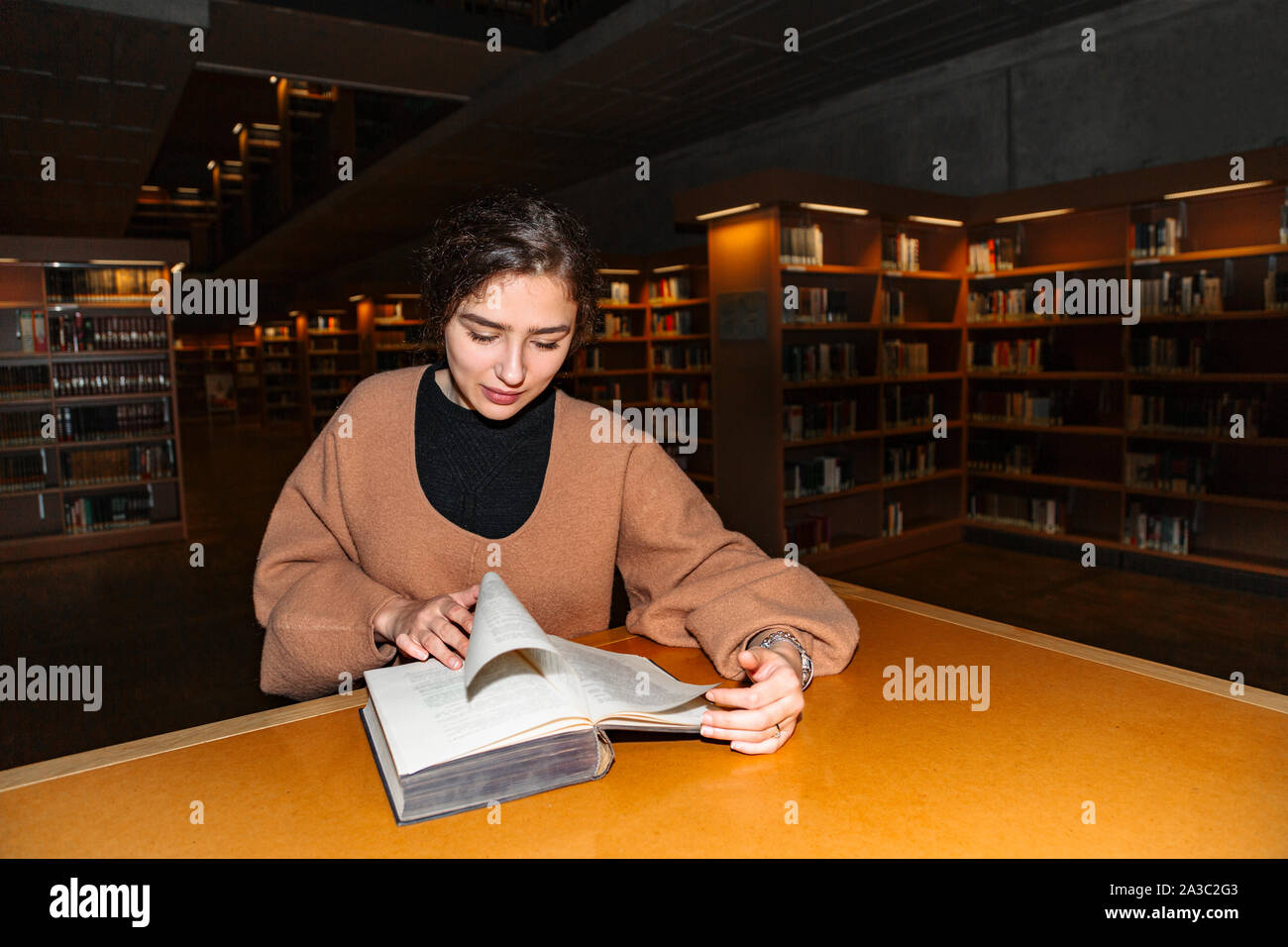 Girl in library turns page of book with smile Stock Photo - Alamy