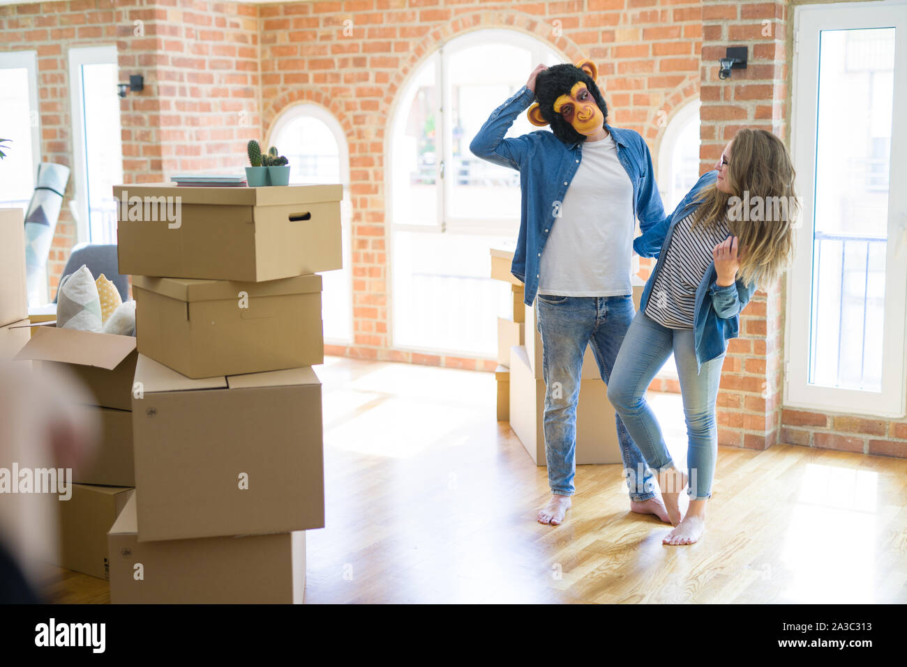 Young couple having fun wearing a monkey mask moving to a new apartment ...
