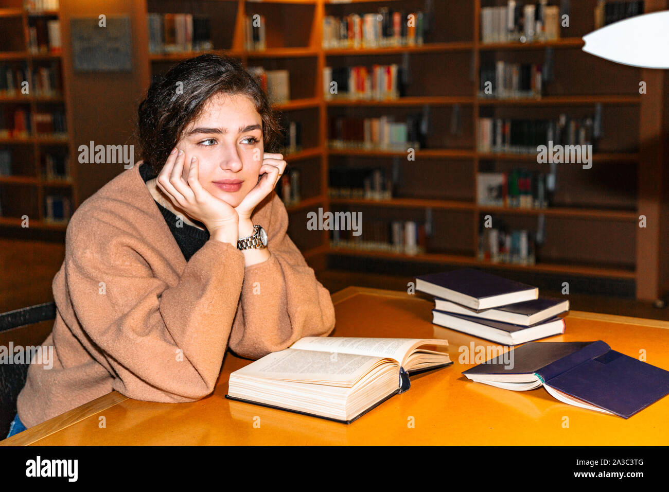 Girl in library sitting over books and thinking Stock Photo - Alamy