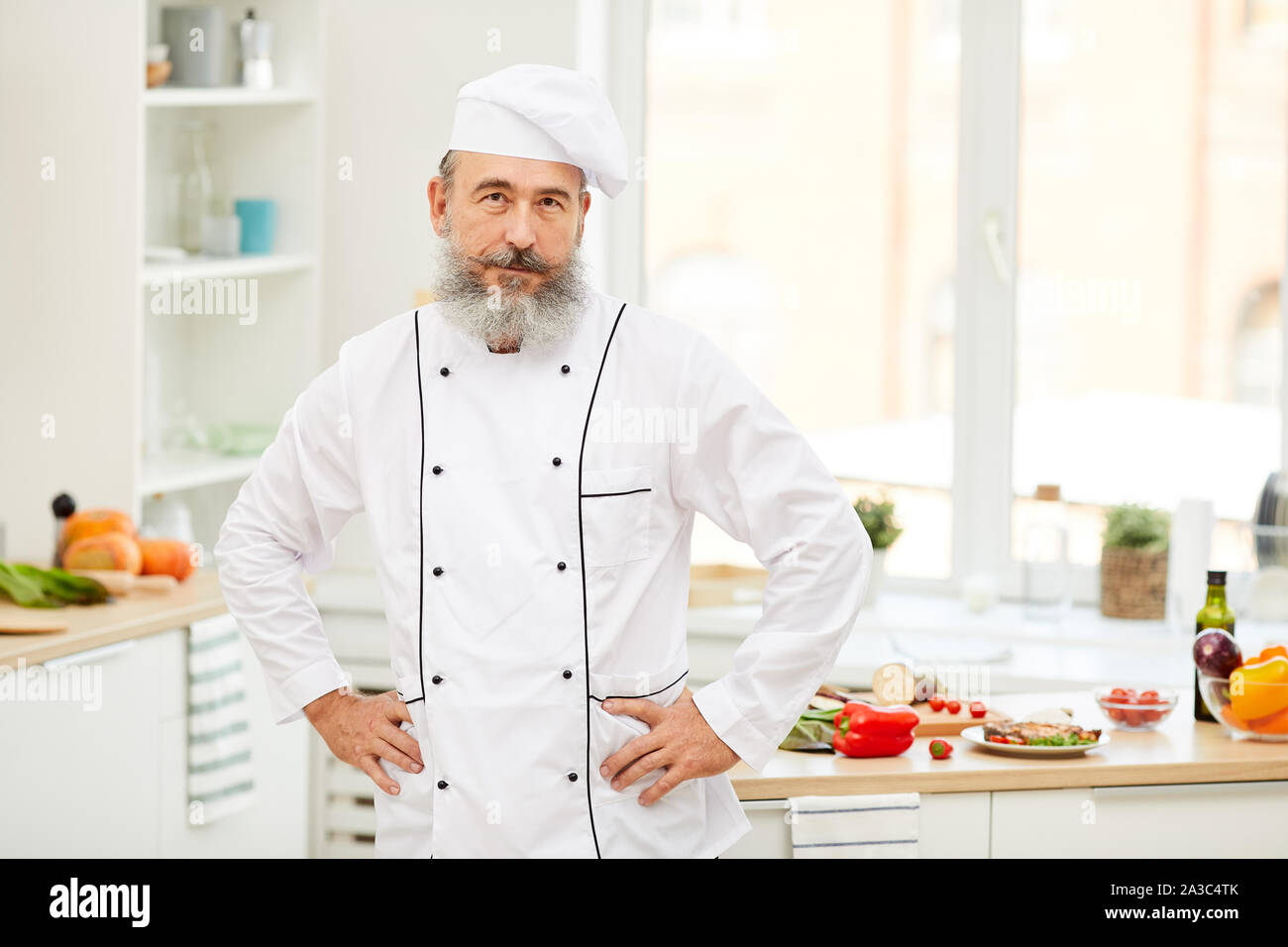 Waist up portrait of bearded senior chef looking at camera while posing ...
