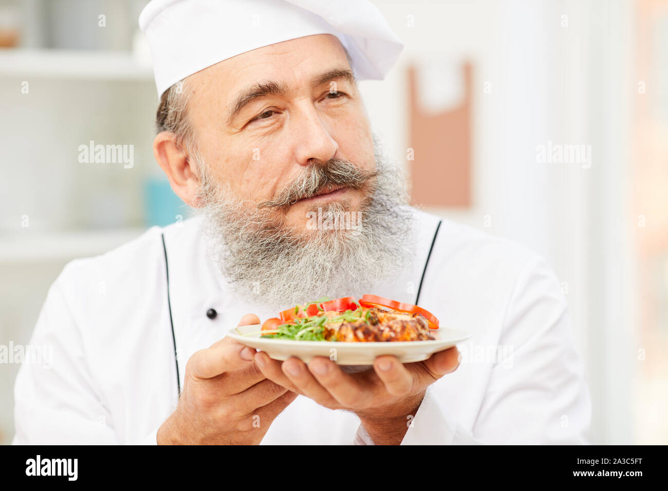 Portrait of blissful senior chef presenting meat steak while cooking in ...