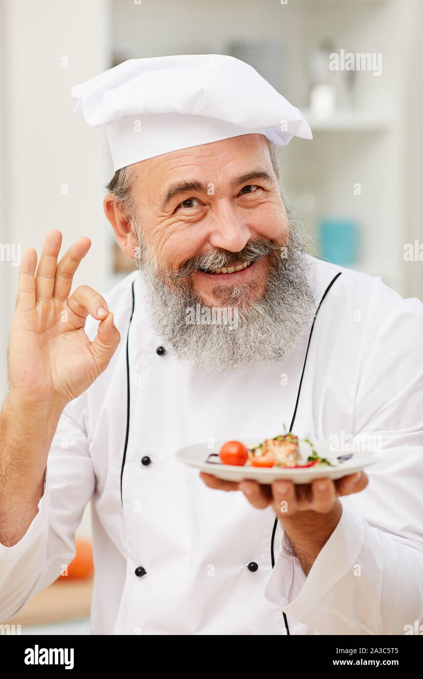 Portrait of bearded senior chef presenting beautiful Italian dish and ...