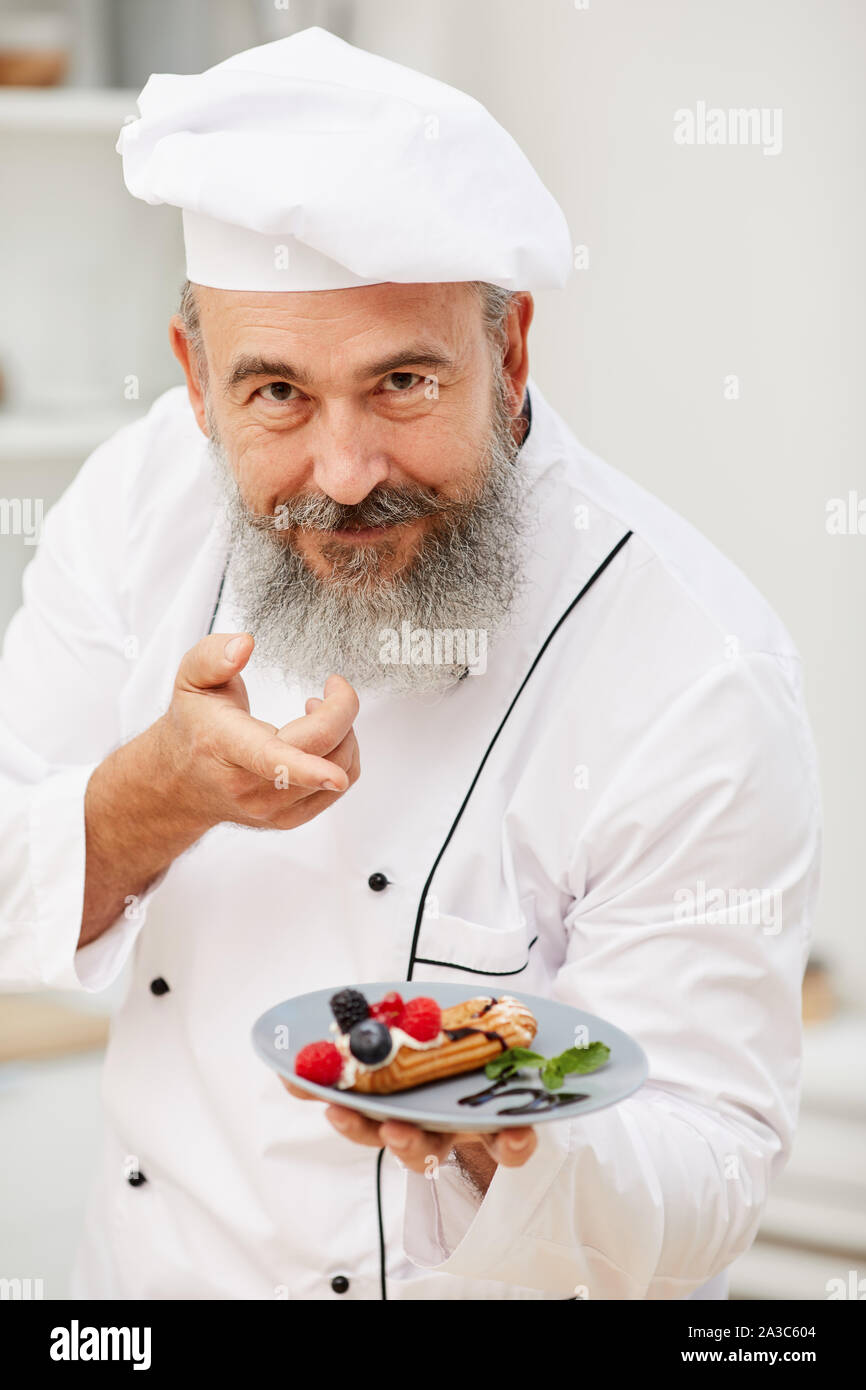 Portrait of bearded senior chef presenting beautiful dessert and ...