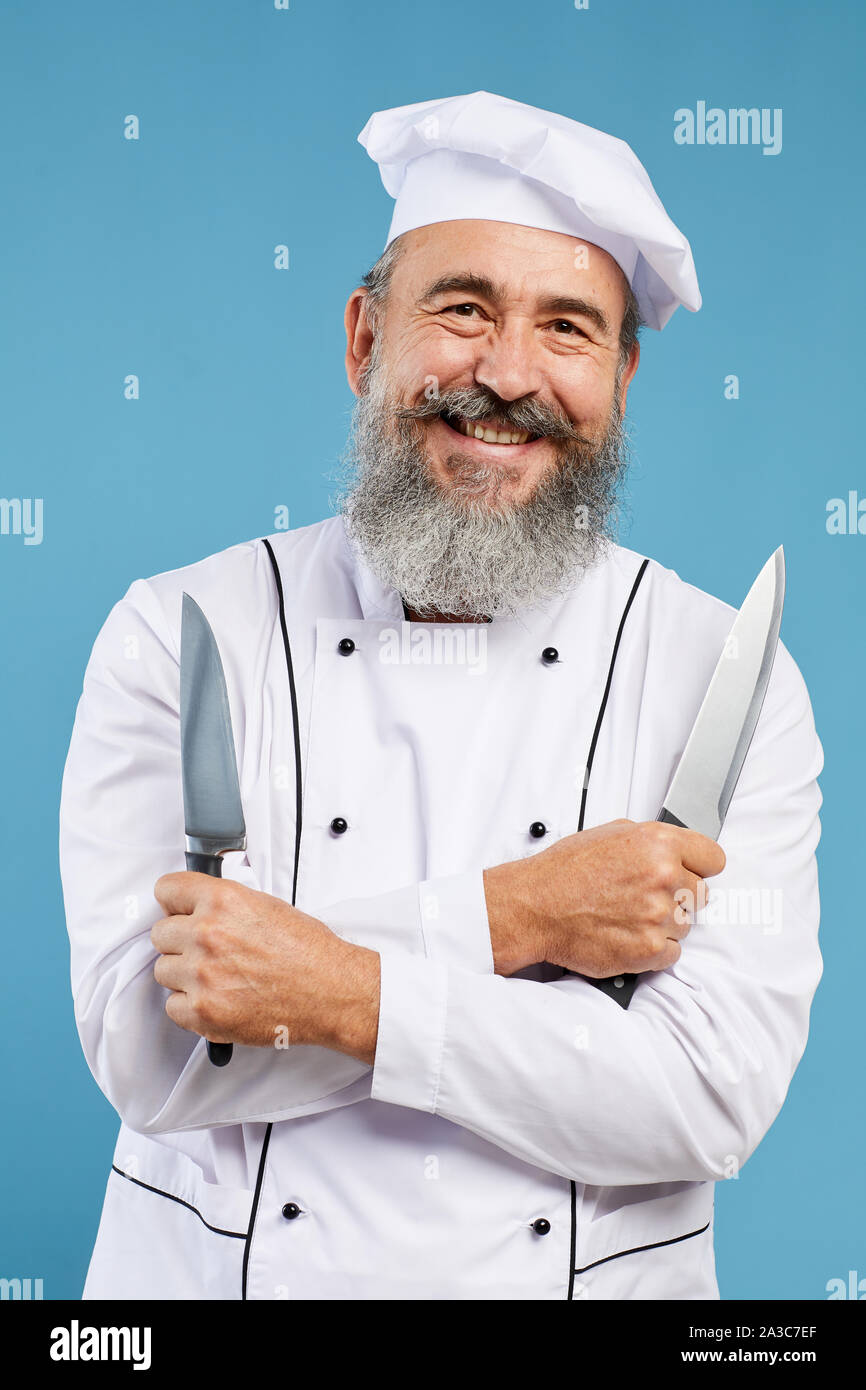 Waist up portrait of charismatic bearded chef holding two knives while ...