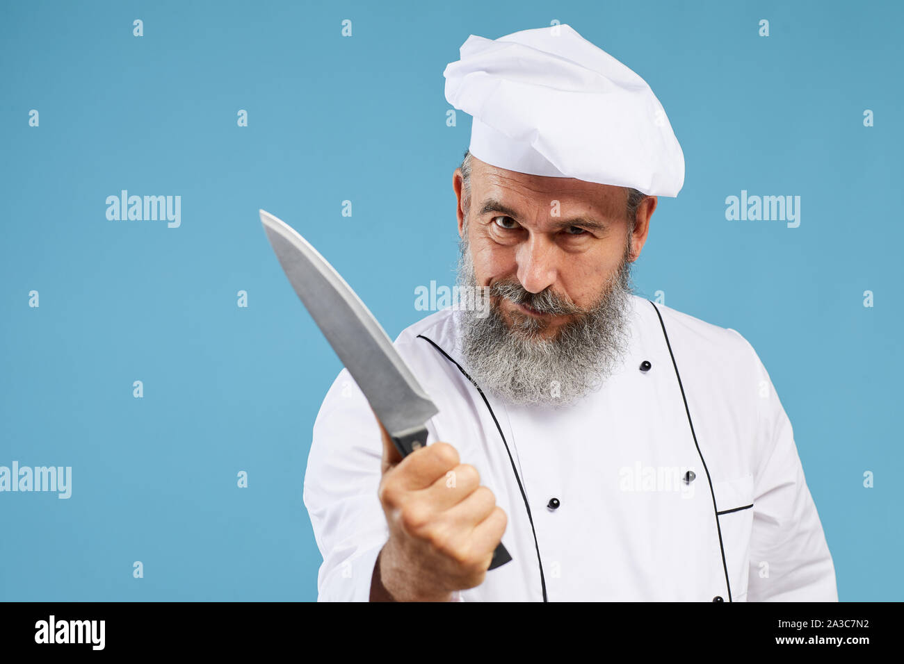 Portrait of bearded senior chef holding sharp knife and looking at ...