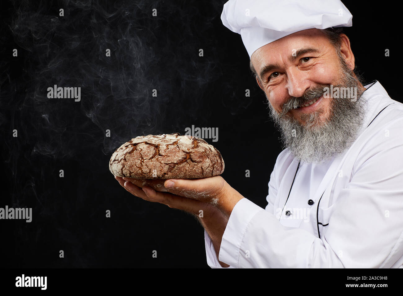 Portrait of charismatic bearded baker holding fresh bread loaf while ...