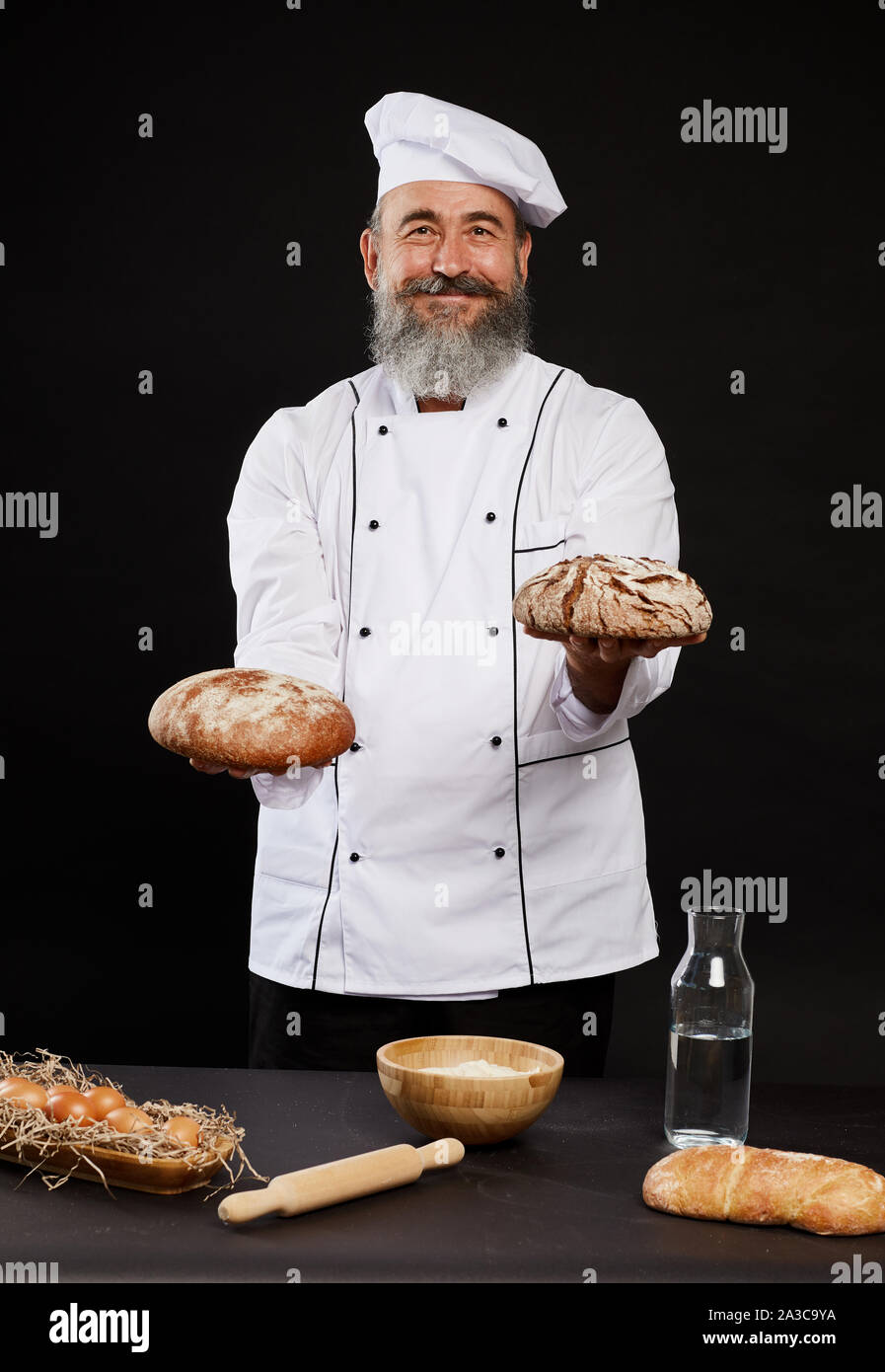 Portrait of bearded baker holding fresh bread smiling happily at camera ...