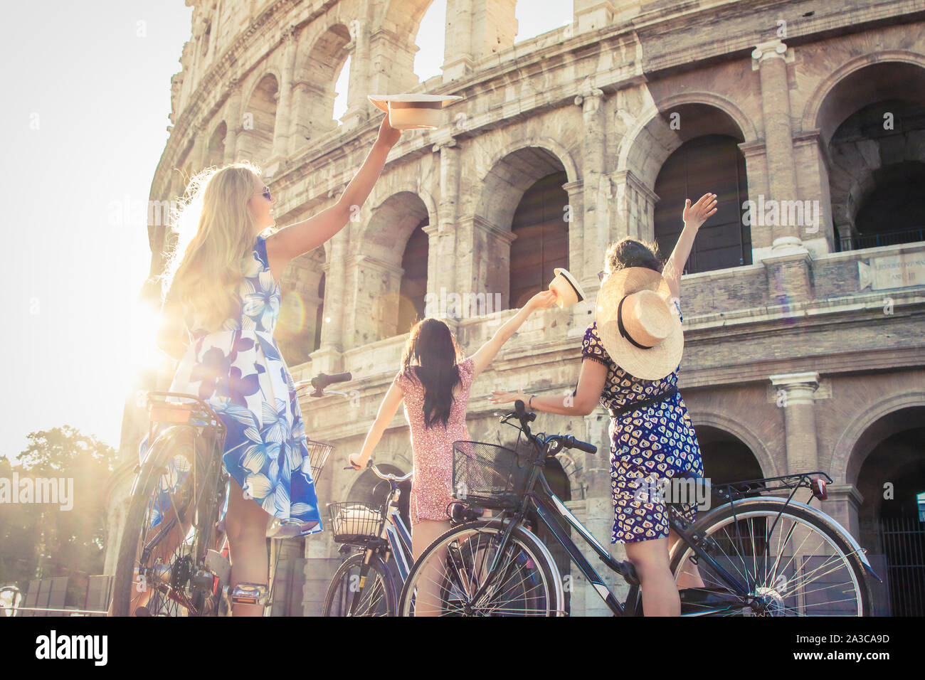 Three happy young women friends tourists with bikes waving hats at ...