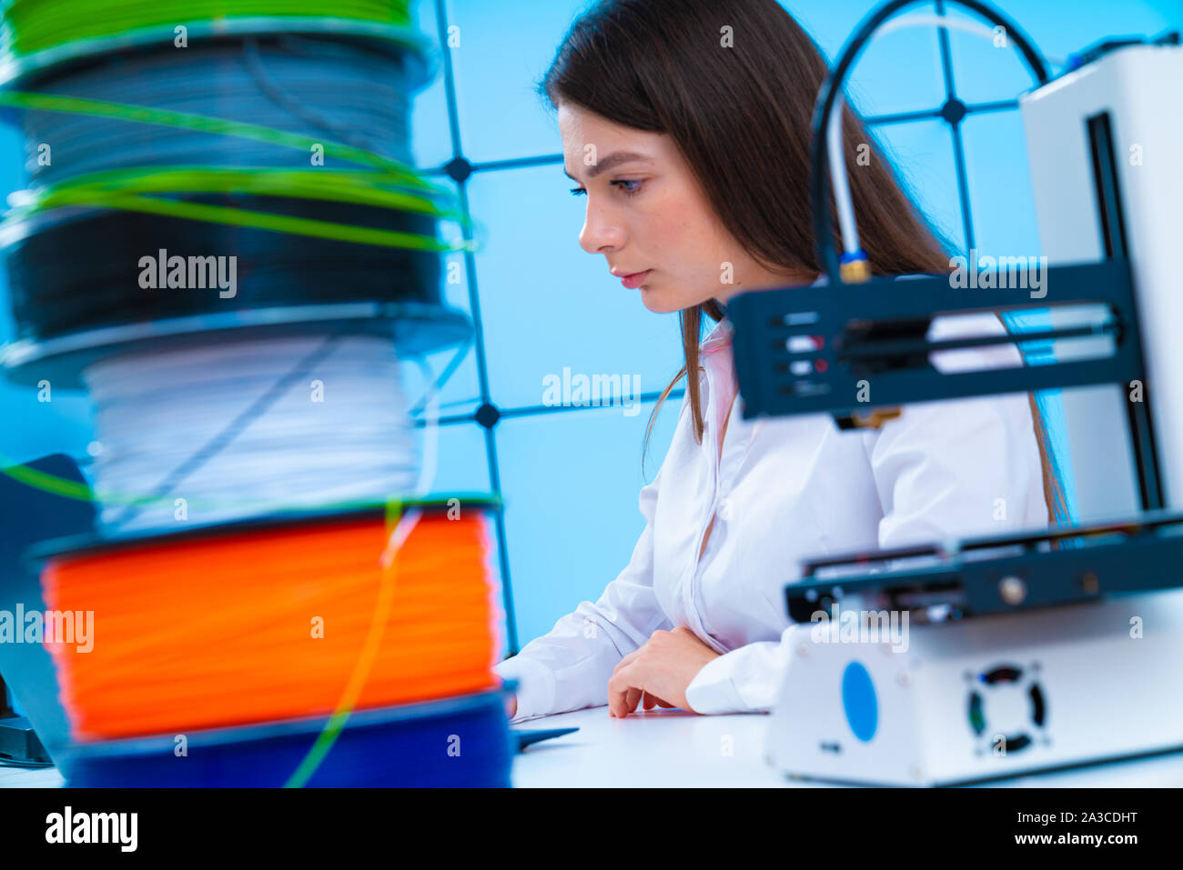 Young woman in design office with 3d printer and plastic filament ...