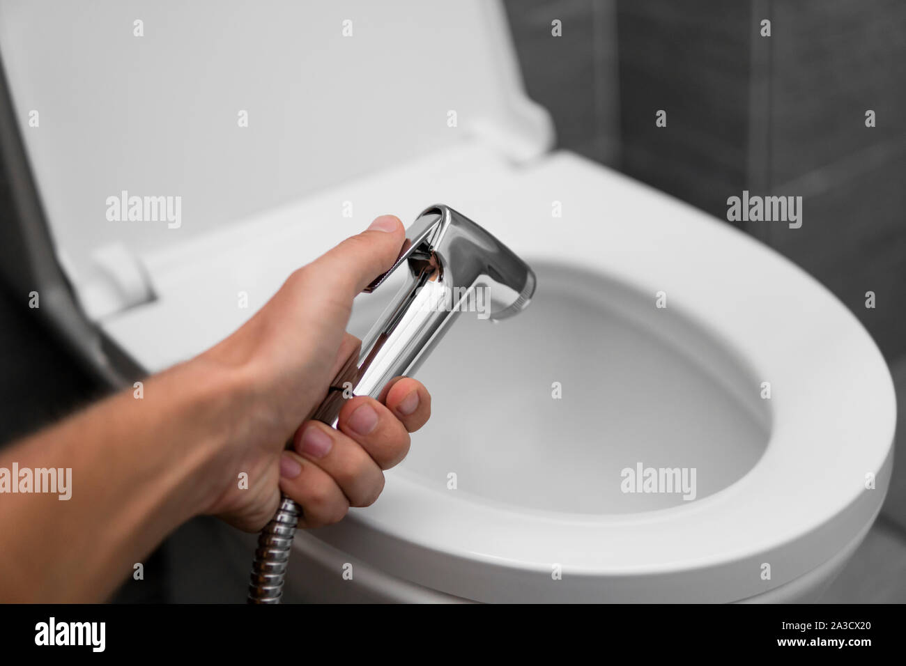 Using of bidet shower with a white toilet. Bidet shower in male hand ...