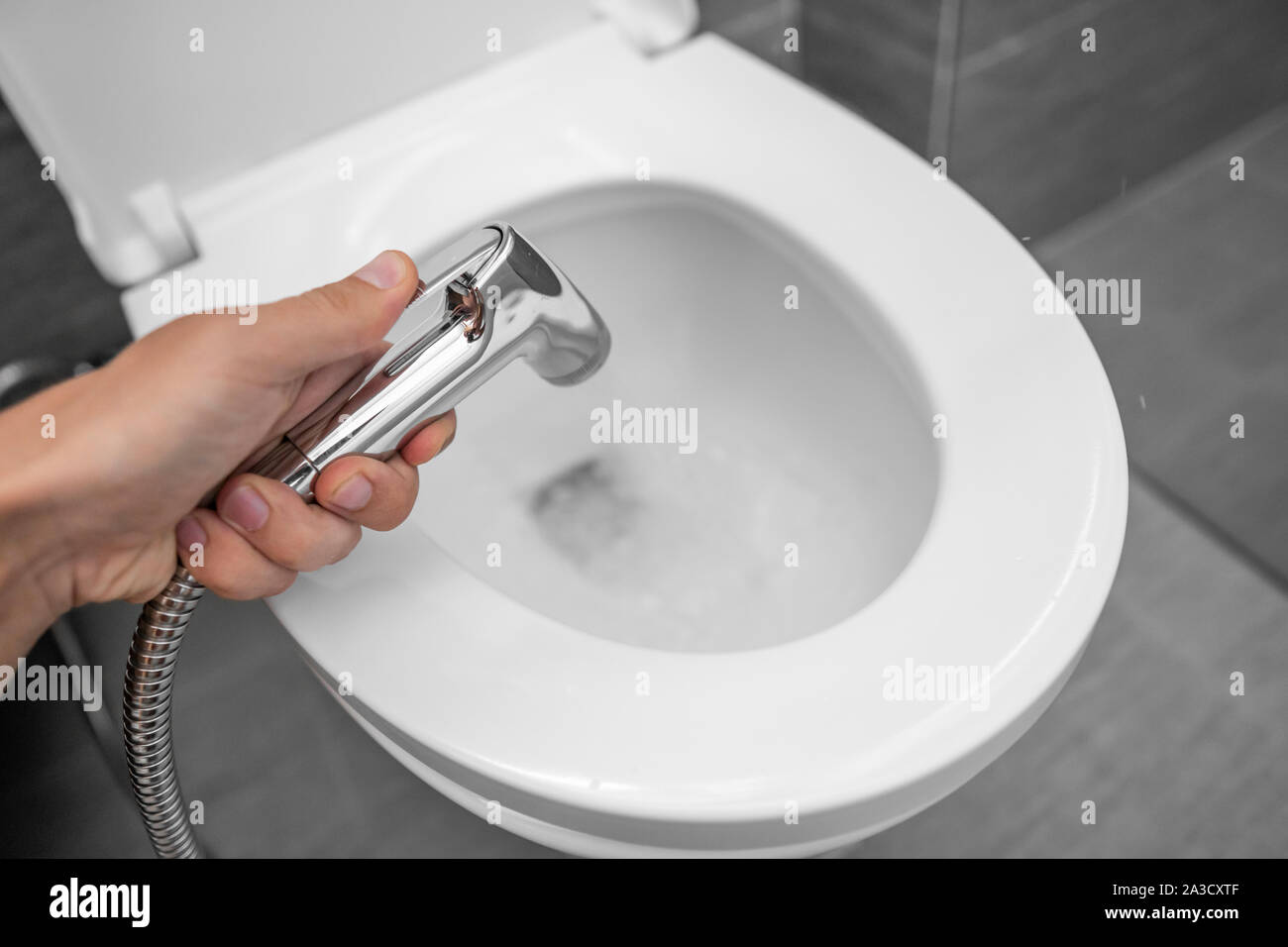 Using of bidet shower with a white toilet. Bidet shower in male hand ...
