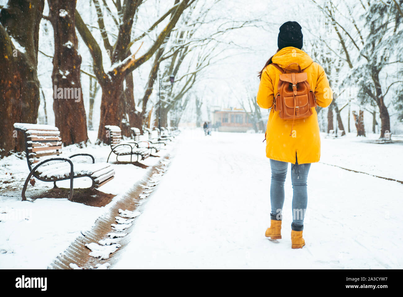 woman walking by snowed city park. view from behind. backpack Stock ...