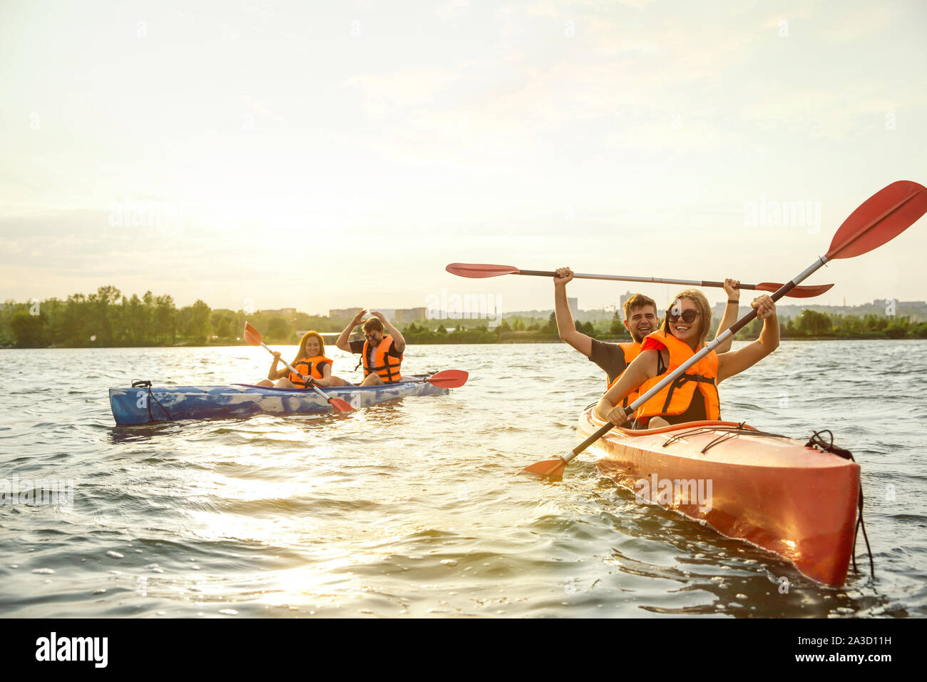 Happy young caucasian group of friends kayaking on river with sunset in ...