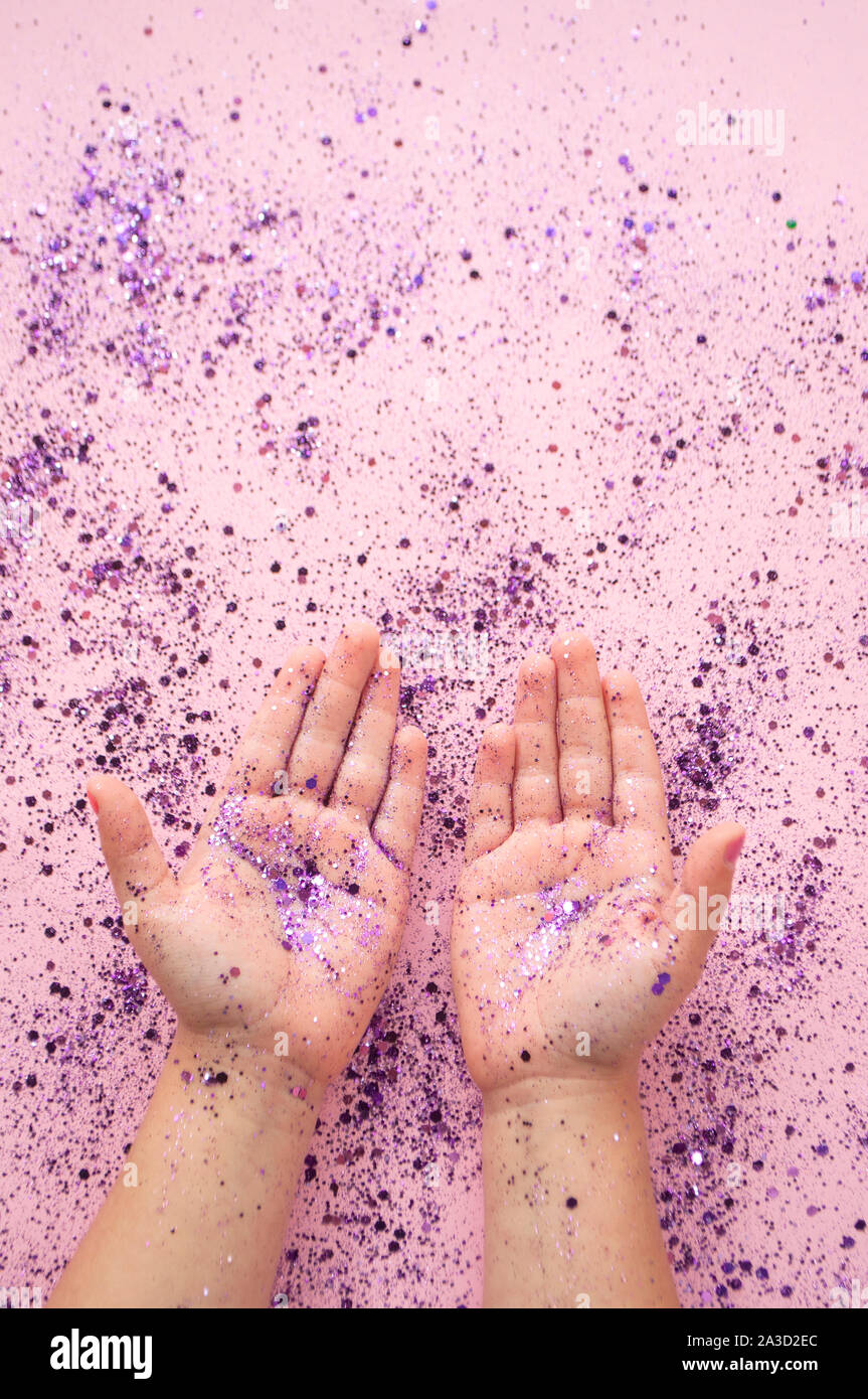 Child's hands with purple color sparkles on pastel pink background ...