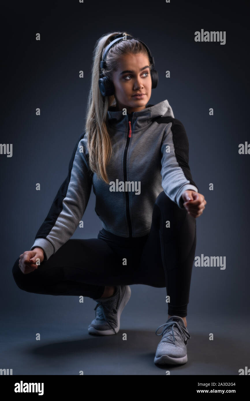 A young blonde girl in sports gear on a dark background adopts various ...