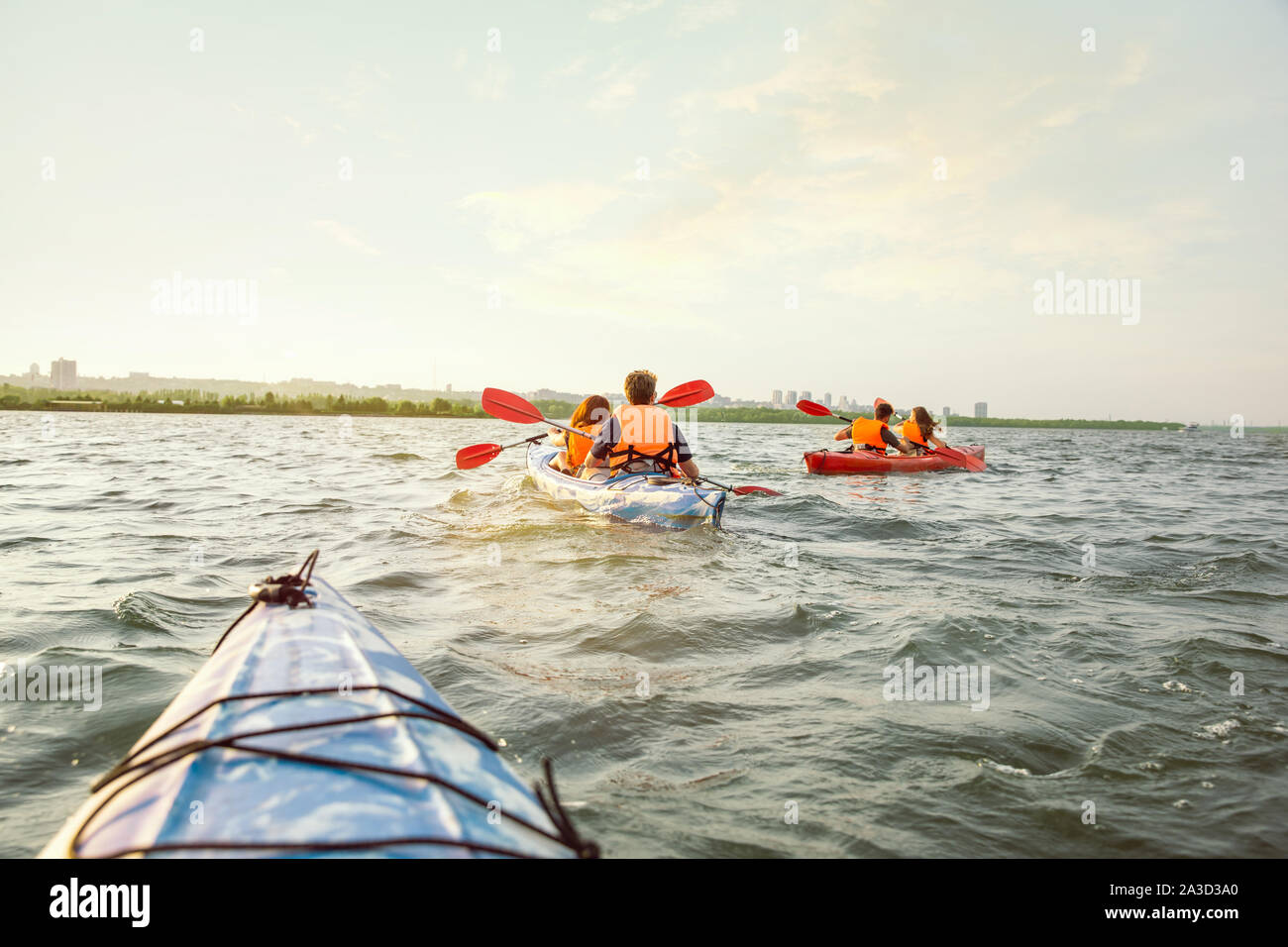 Happy young caucasian group of friends kayaking on river with sunset in ...