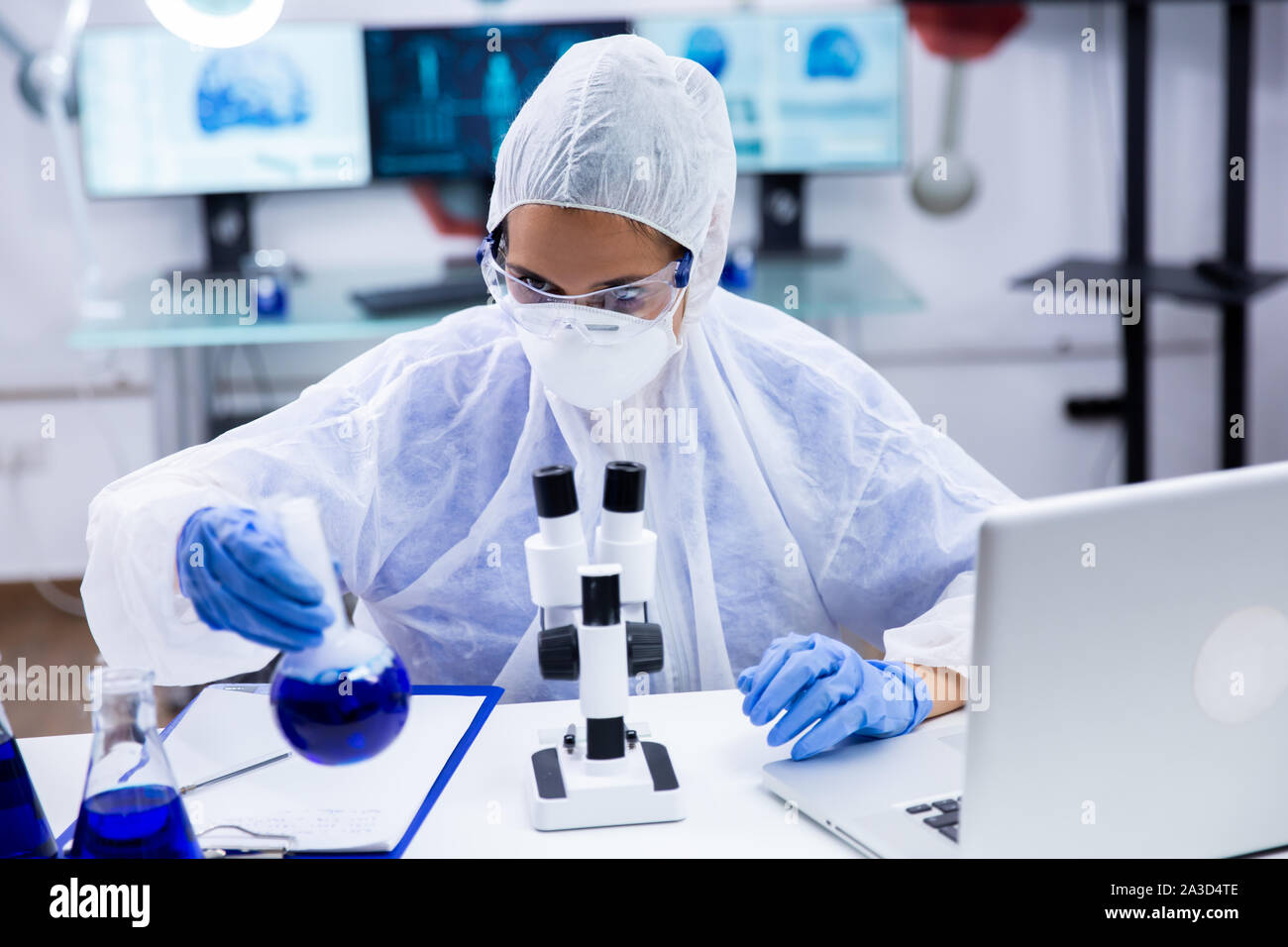 Caucasian Scientist sitting down shakes a tube with a blue substance ...