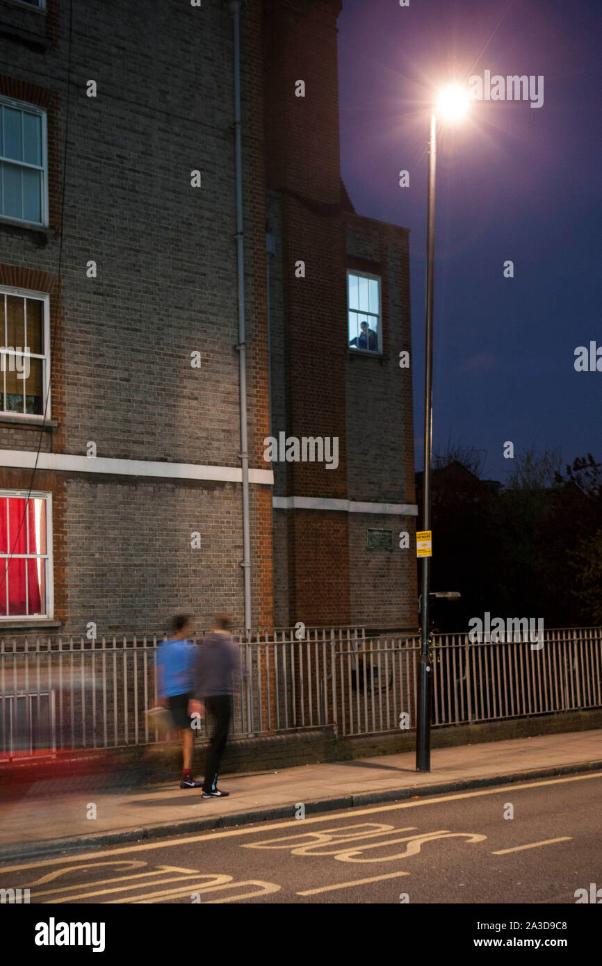 Men walk past lamppost with a figure reading in a window above Stock ...