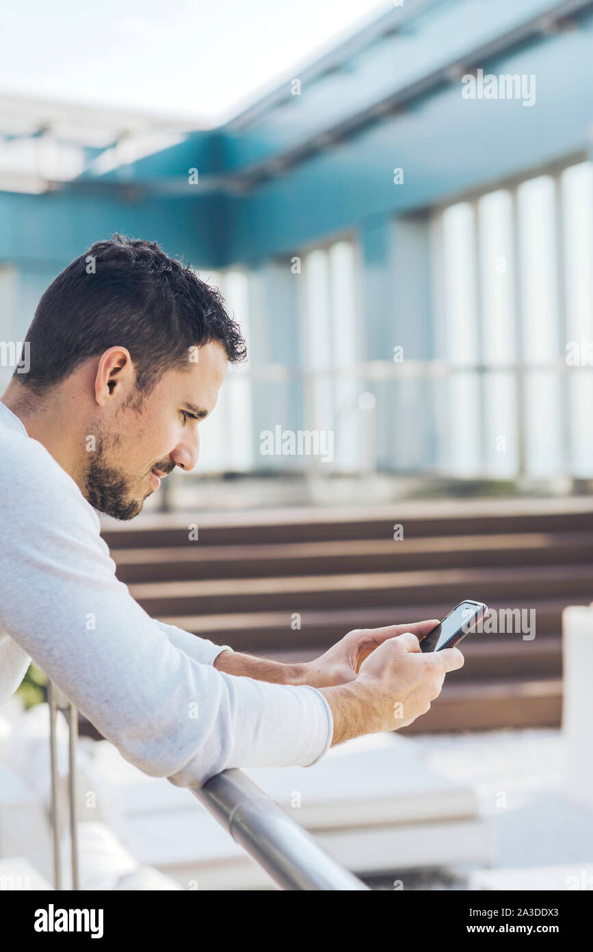 Young man leaning on railing while using mobile phone Stock Photo - Alamy