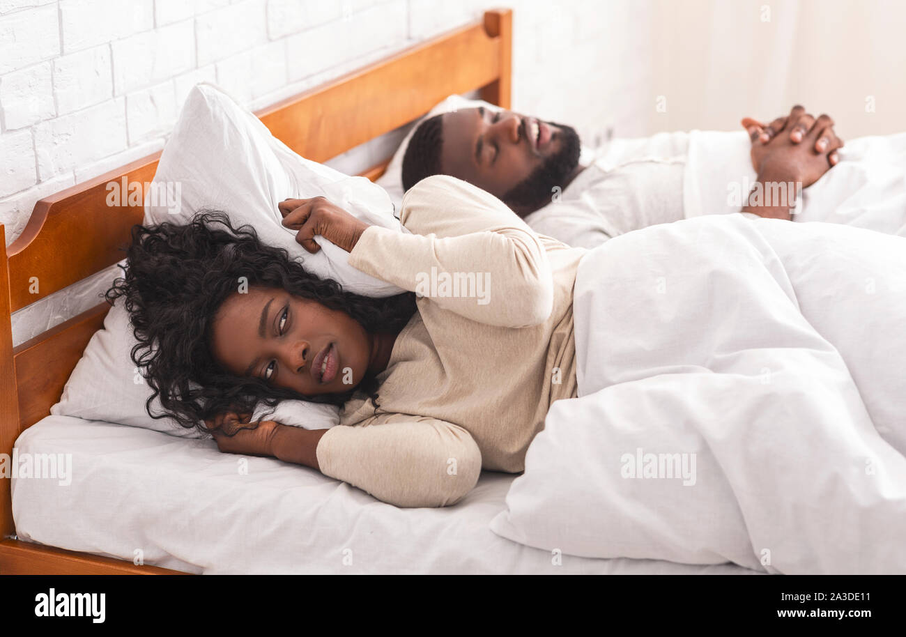 Black woman suffering from snoring boyfriend, closing ears with pillow ...