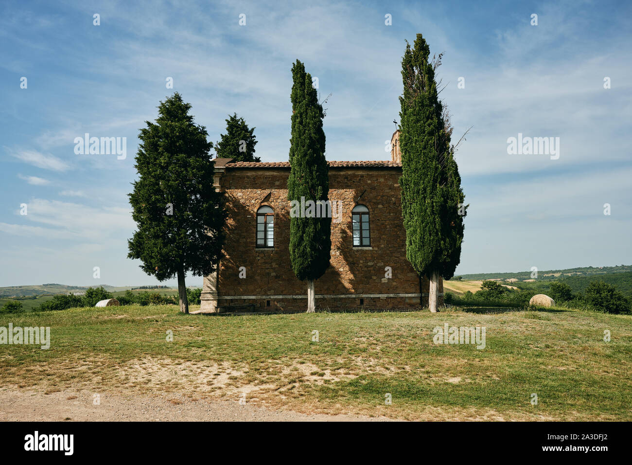 High trees growing in row around small aged bricked house of chapel in ...