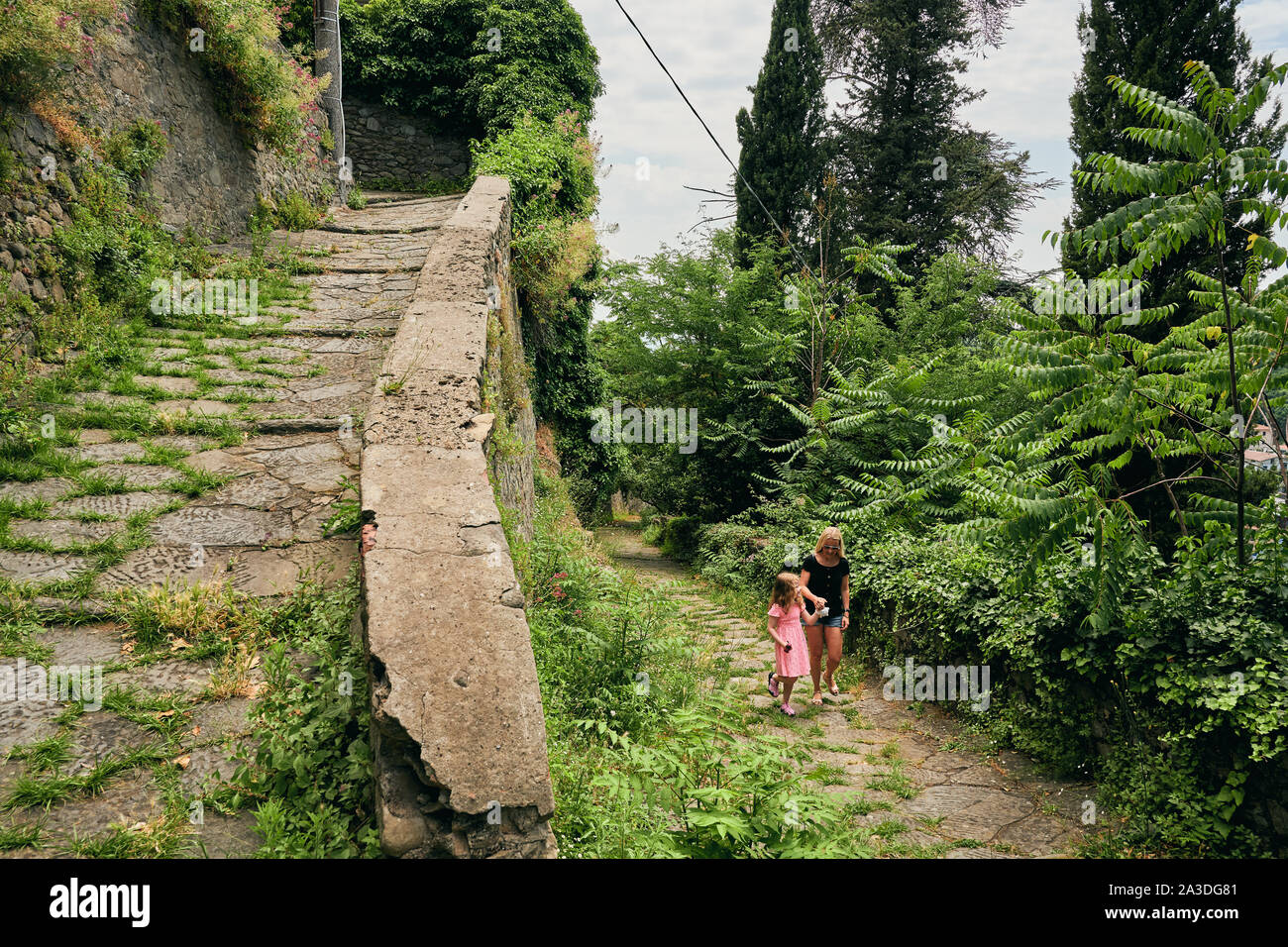 Carefree woman and girl holding hands and strolling along grassy path ...
