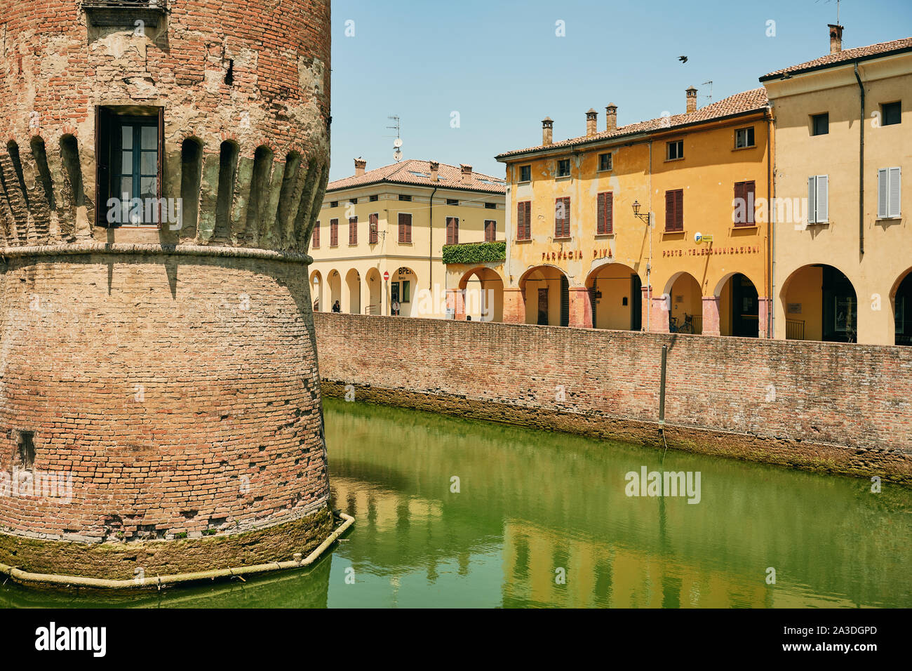 Round brick tower and green water in canal flowing along street with ...