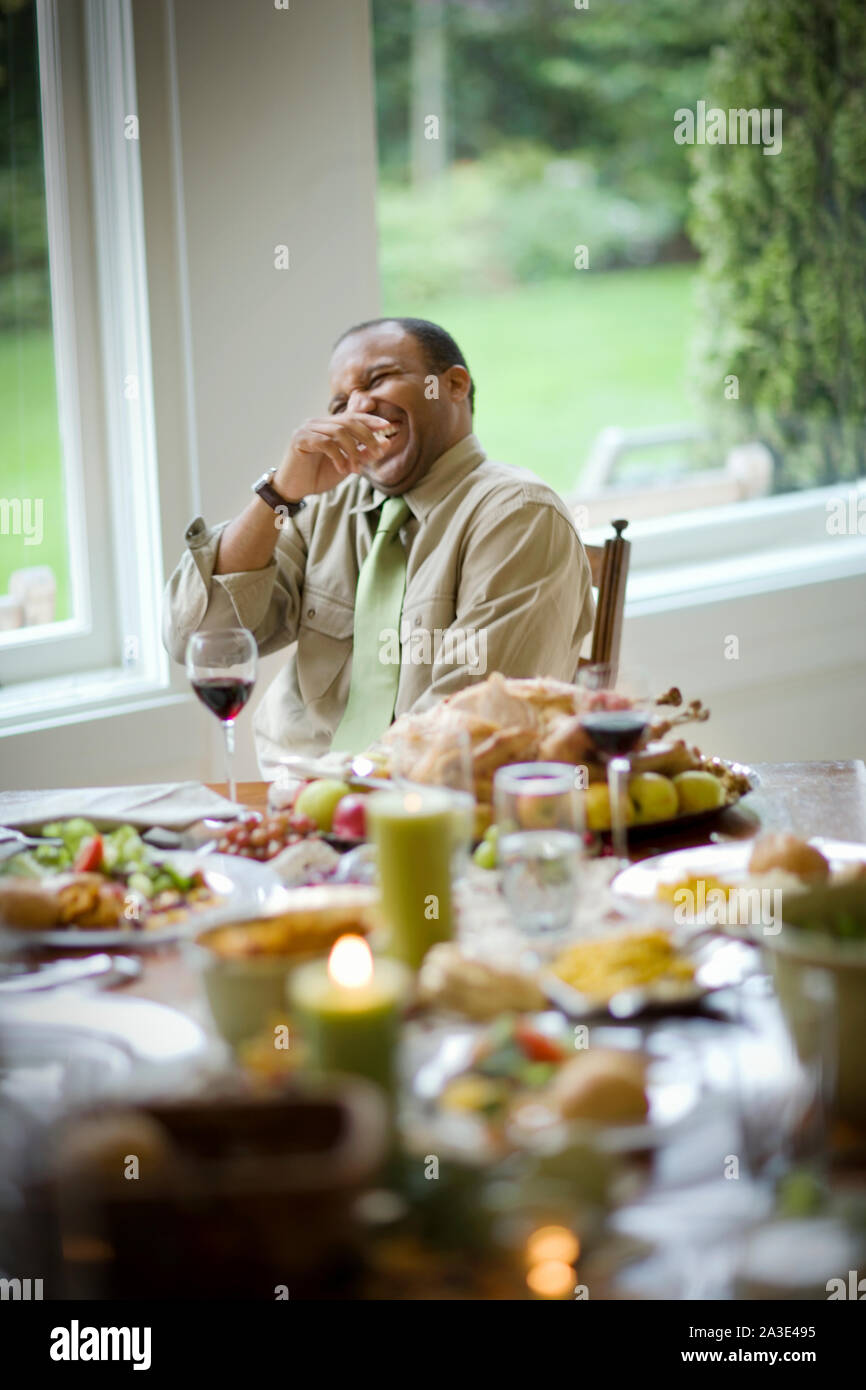 Mid-adult man laughing while seated at the head of a dining table Stock ...