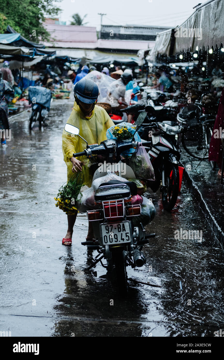 Vietnamese prepares his scooter in the rain. Hoi An Central Market ...