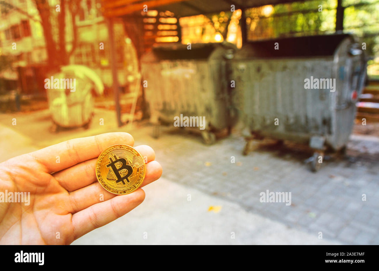 Hand holding a golden bitcoin , blurred background of trash , recycling ...