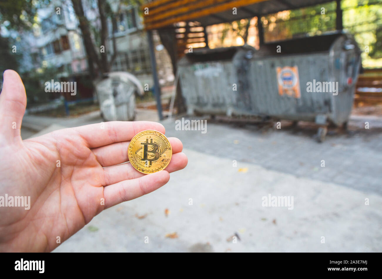 Hand holding a golden bitcoin , blurred background of trash , recycling ...