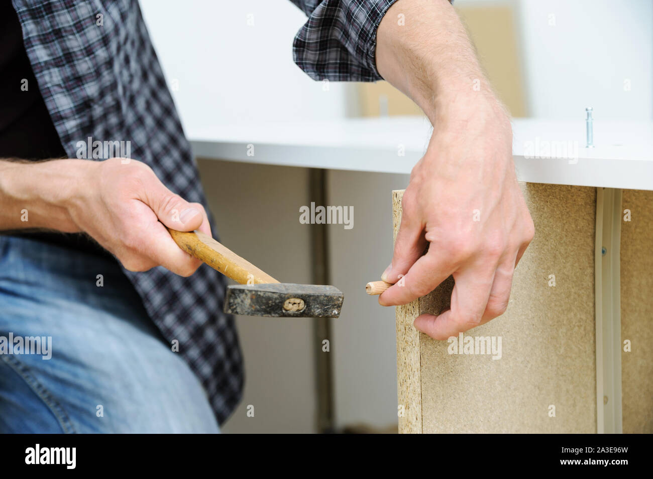 A man is hammering a wooden pin into a furniture board Stock Photo - Alamy