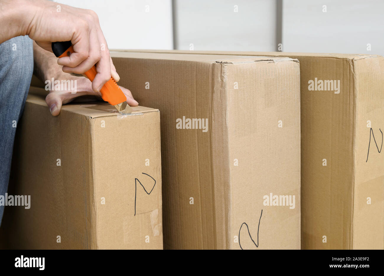 A man is unpacking the cardboard boxes. He is cutting the adhesive tape ...
