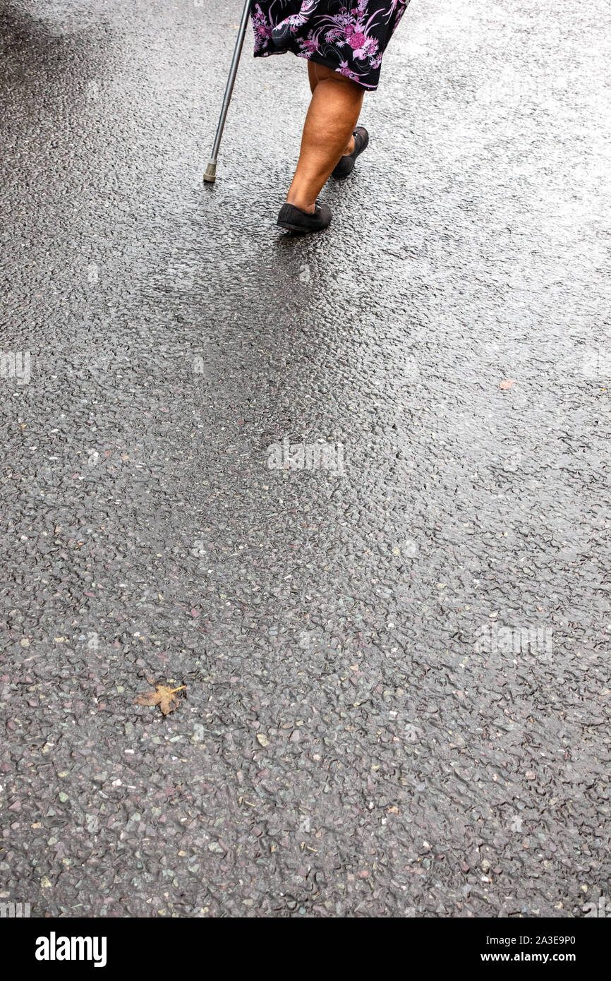Lower part of older lady's legs walking on road, using walking stick ...