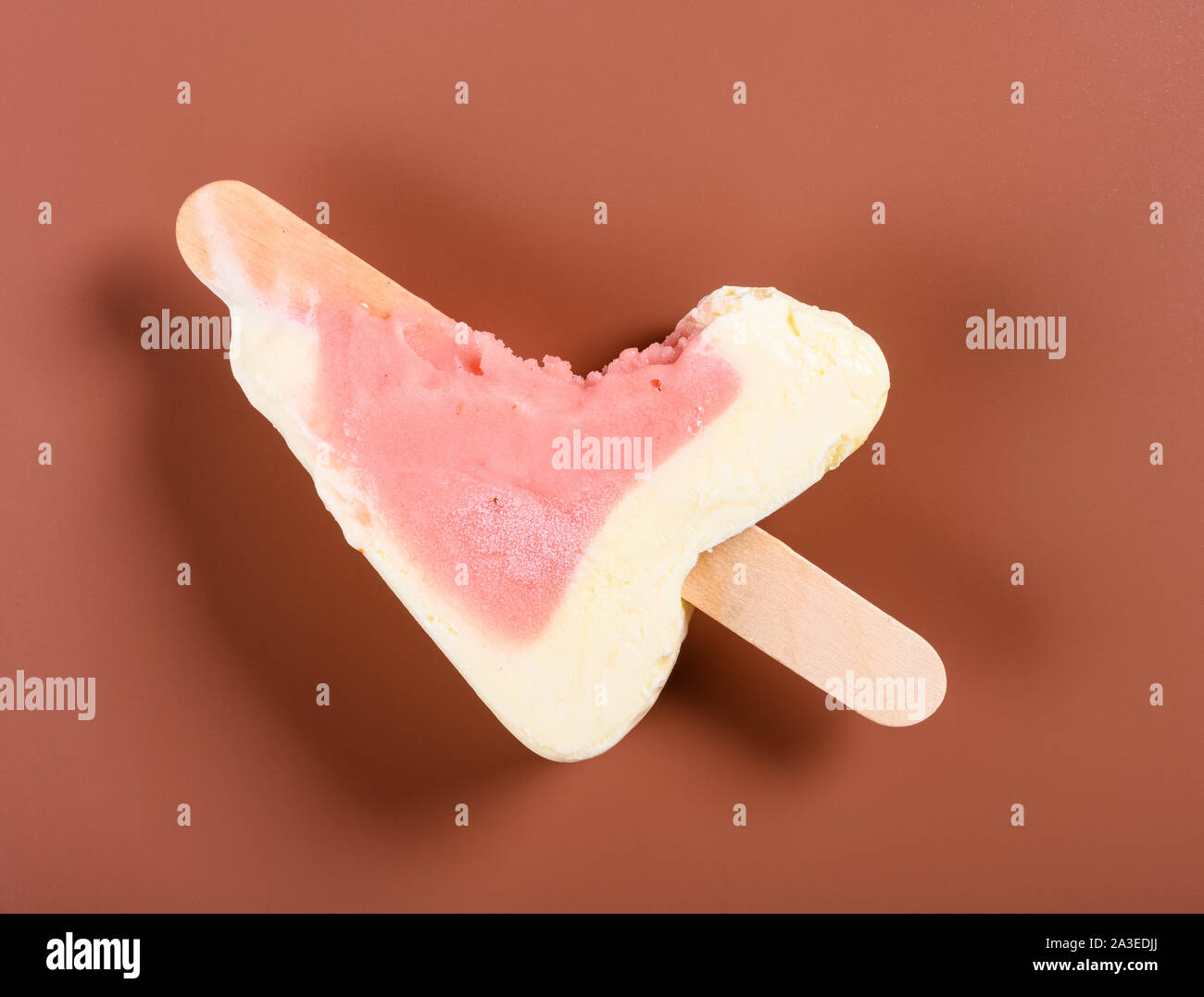 top view half eaten strawberry flavor popsicle on a brown background ...
