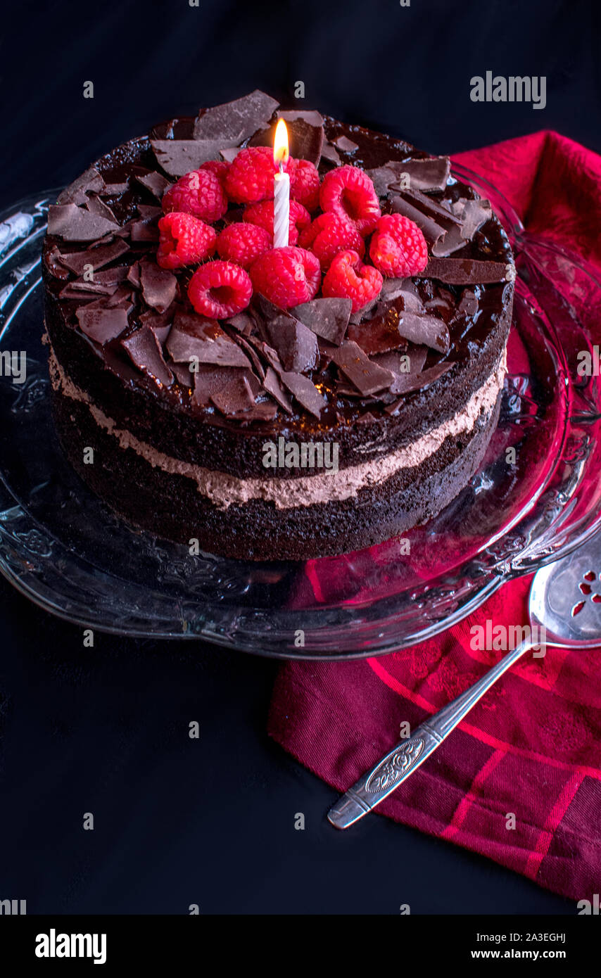 A lit candle atop a delicious chocolate and raspberry cake, is the ...