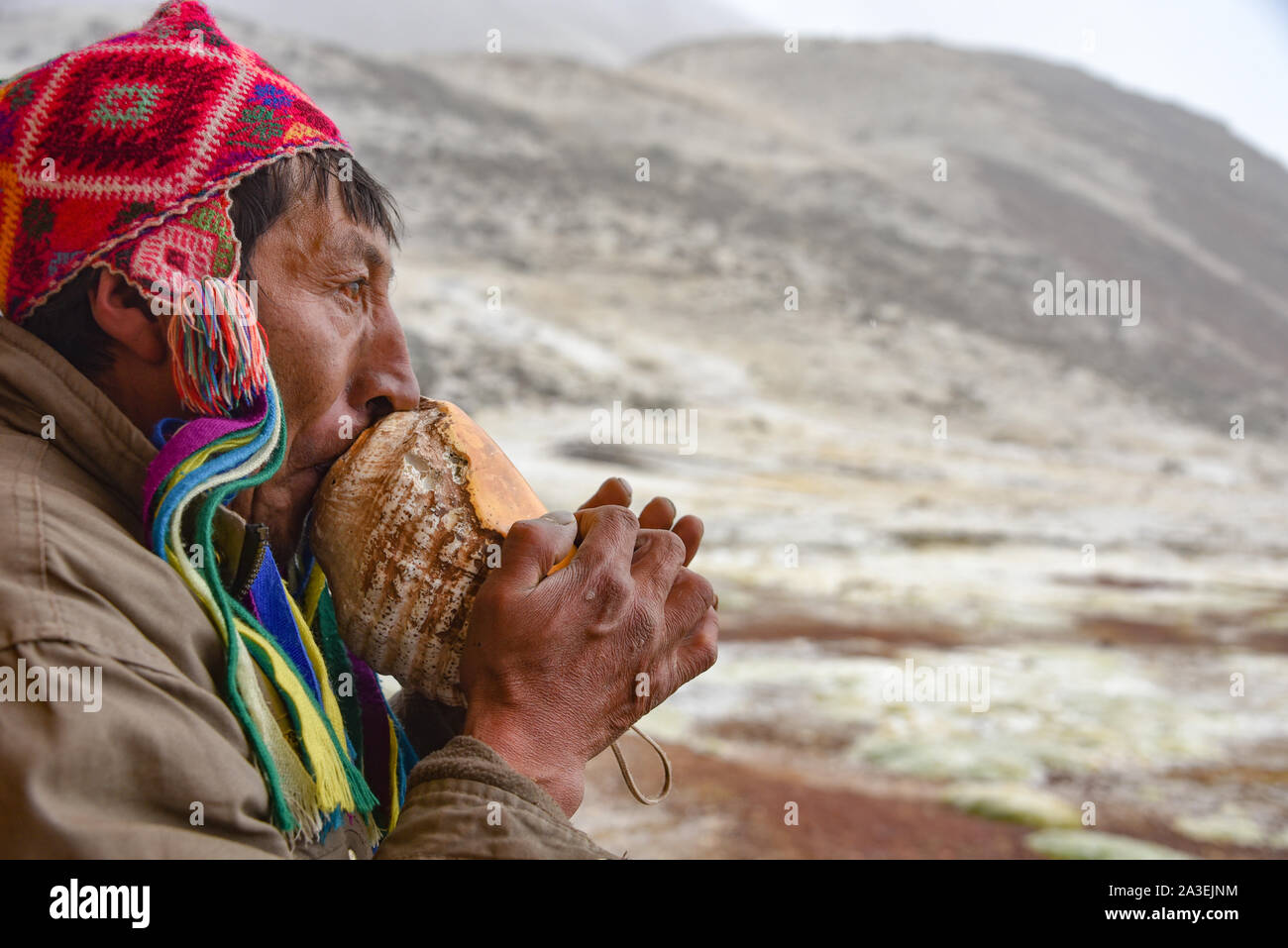A Quechua man in traditional head wear blows on a conch shell to ...