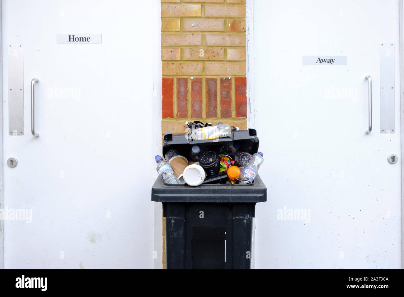 An overflowing rubbish bin ina. football stadium with two doors for the ...